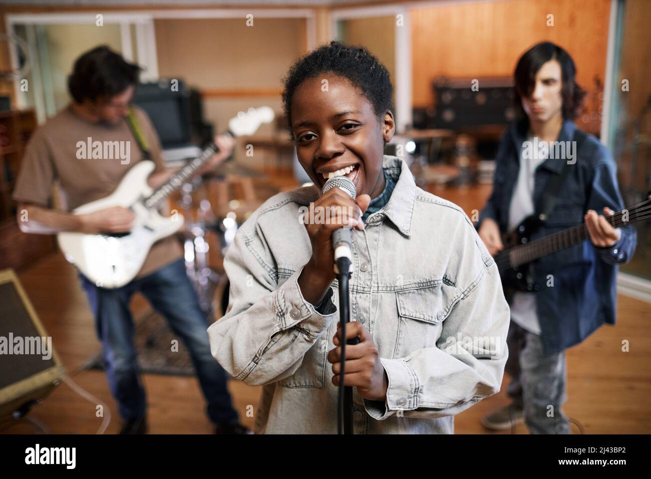 Waist up of black female musician singing to microphone with band in ...