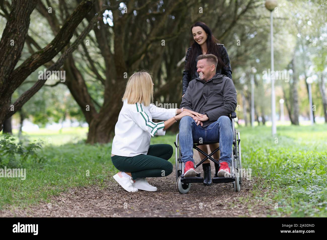 Two women and man in a wheelchair are talking in park Stock Photo - Alamy