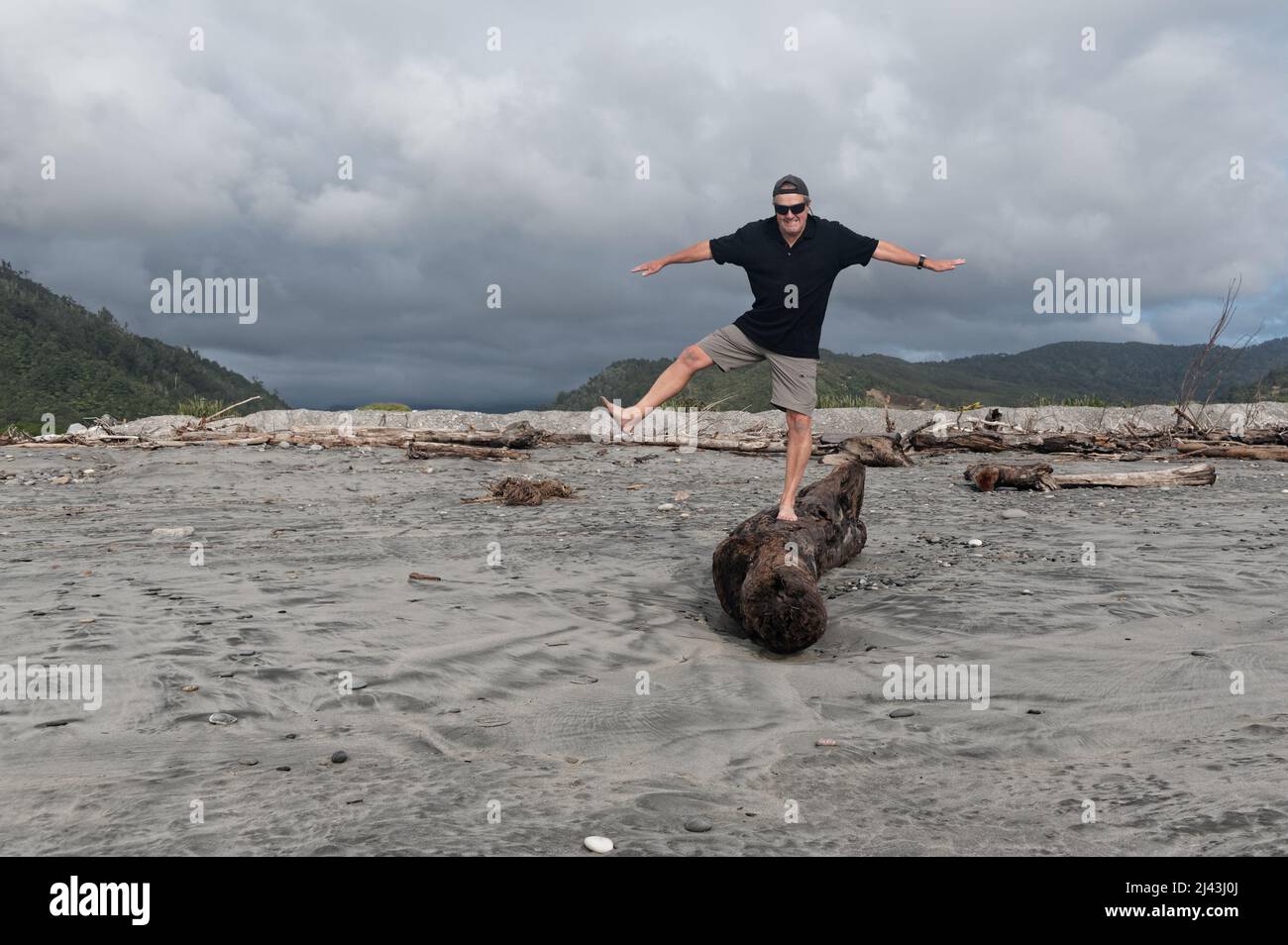 An older man is balancing on one leg while standing on a log on the ...