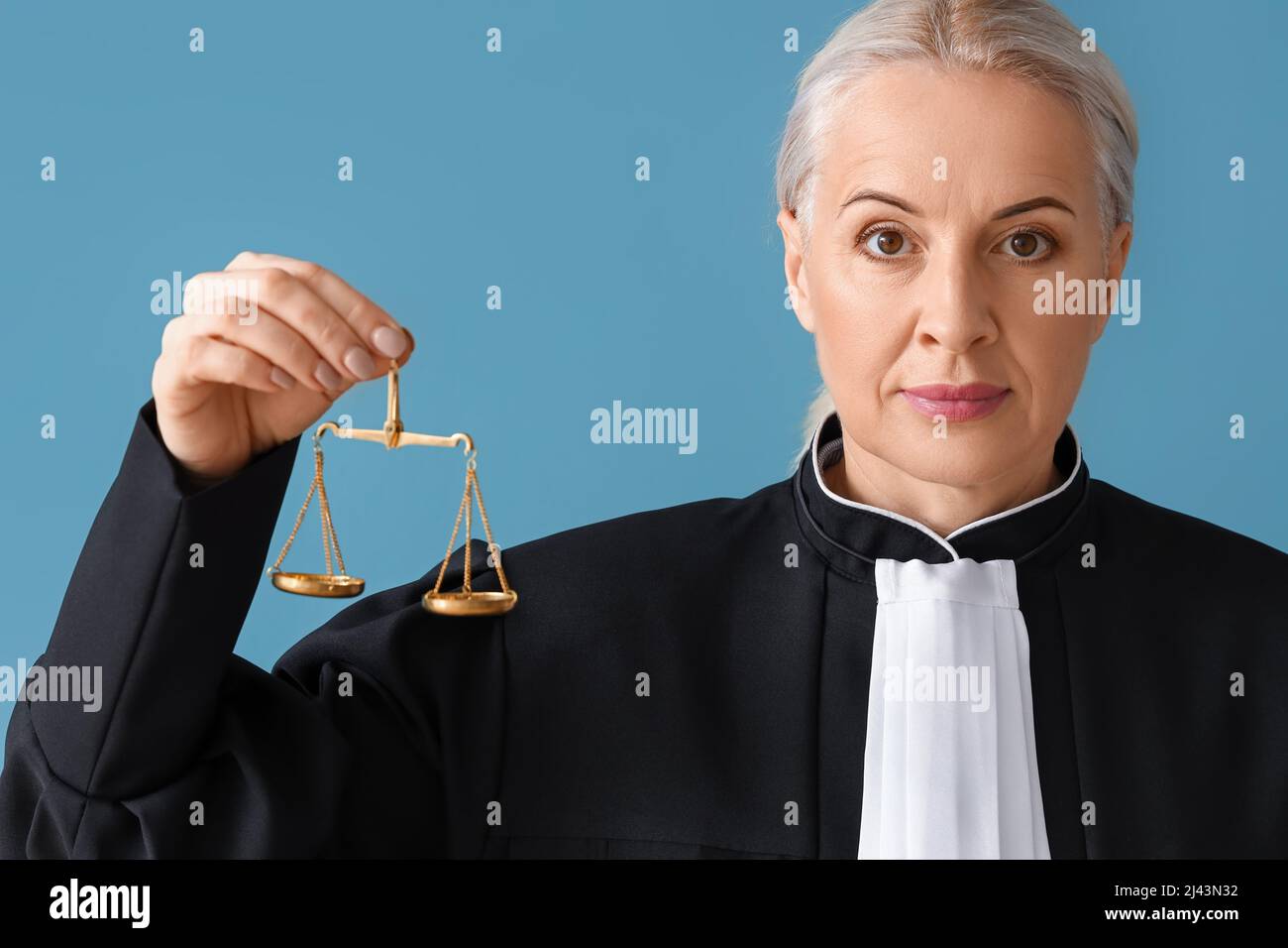 Mature female judge in robe with justice scales on blue background ...