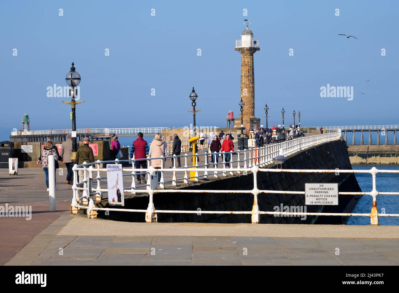 Tourists walk along Whitby Harbour front towards Whitby lighthouse in ...