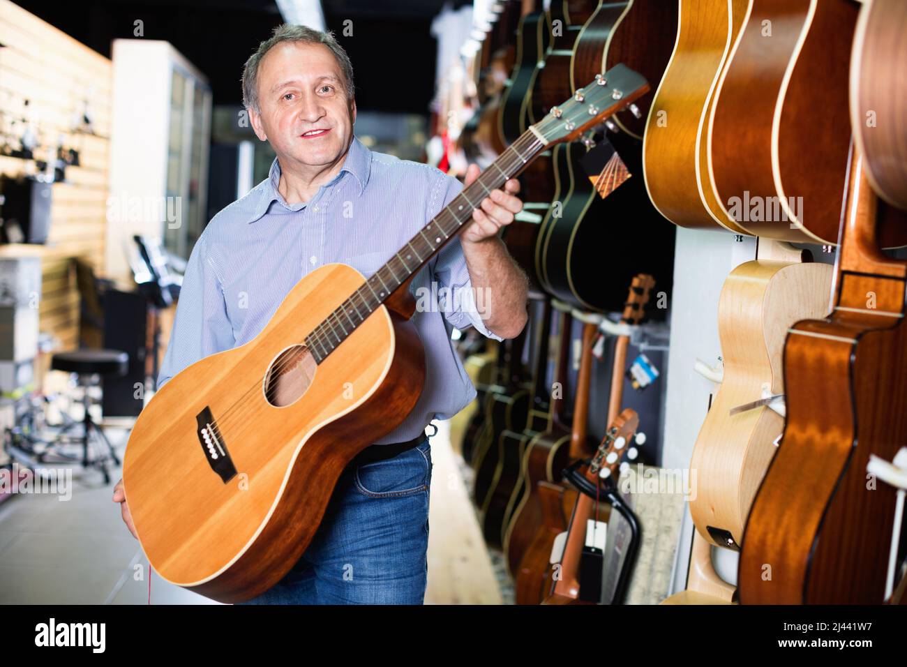 Adult guitarist is standing with acoustic guitar in music store Stock ...