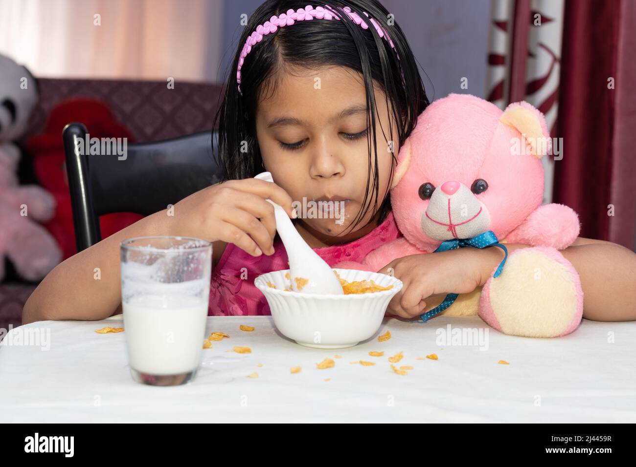 An Indian girl child eating cereal with milk in a domestic room with ...