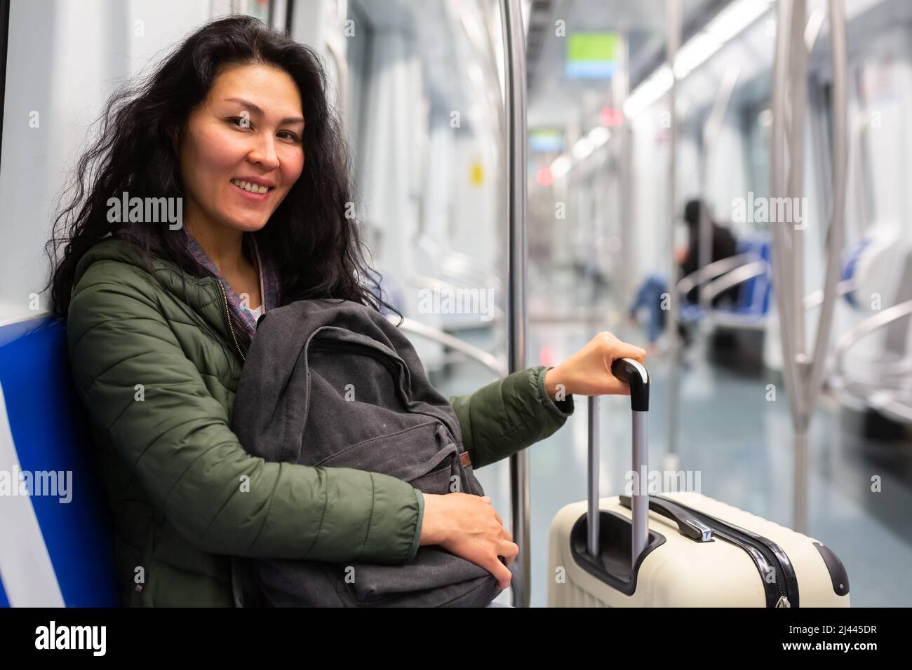Asian positive woman with suitcase sitting in subway car Stock Photo ...