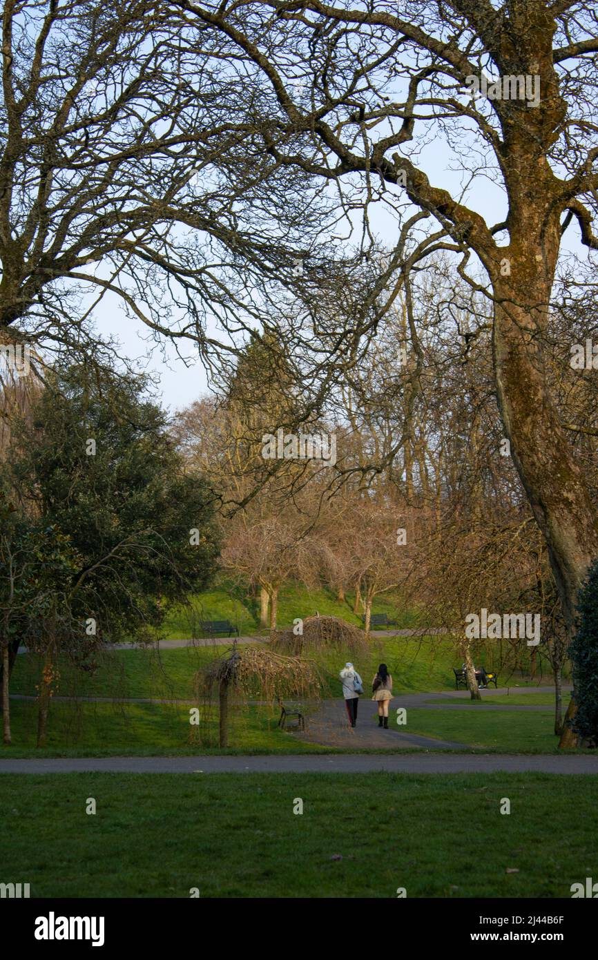 Two girls walking into park path surrounded by trees and greenery Stock ...