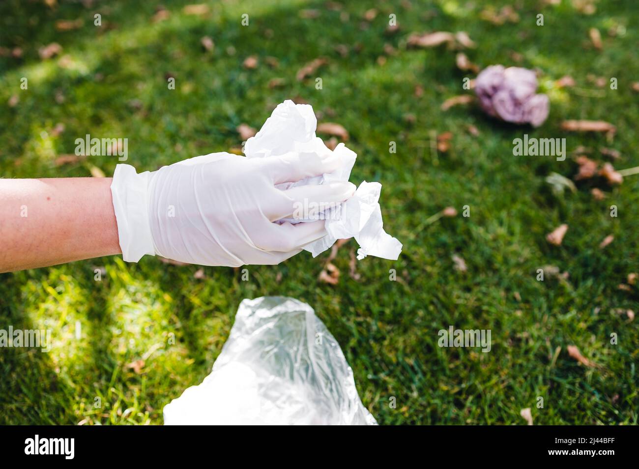 hand grabbing plastic bags and wrappers from green lawn in a park ...