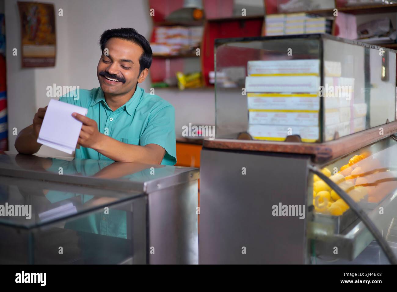 Portrait of happy Sweet shop owner maintaining accounts at counter ...