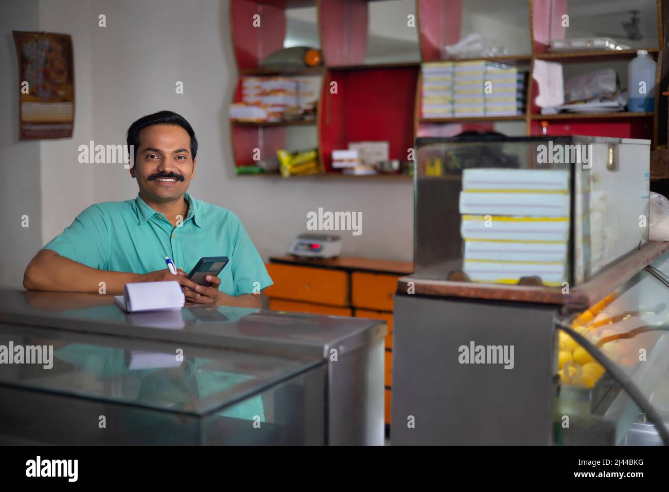 Portrait of Sweet shop owner maintaining accounts by using Smartphone ...