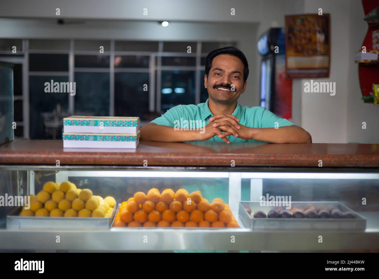 Sweet shop owner looking at camera with smile while standing at counter ...