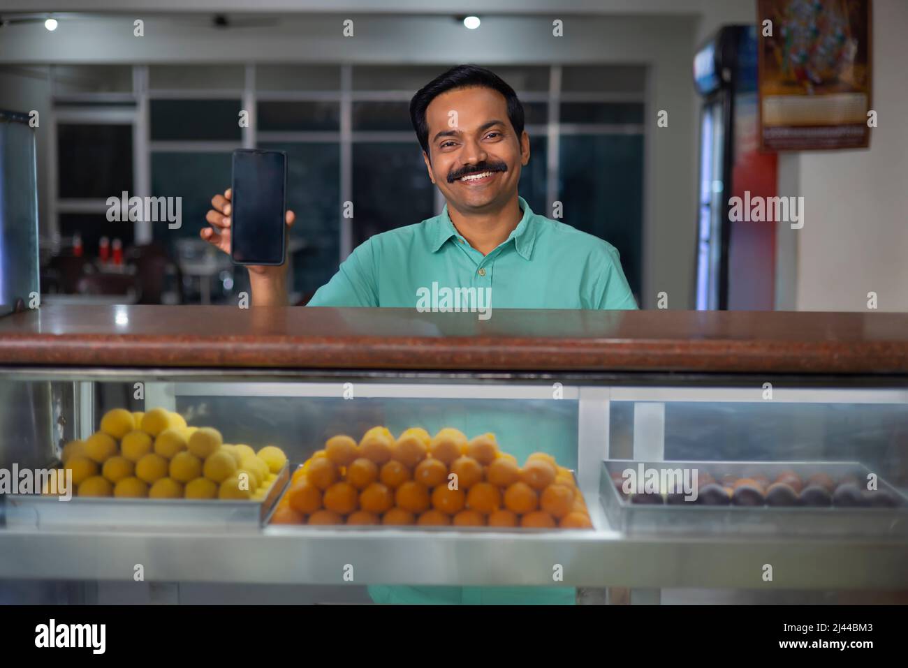 Sweet shop owner displaying Smartphone while standing at counter Stock ...