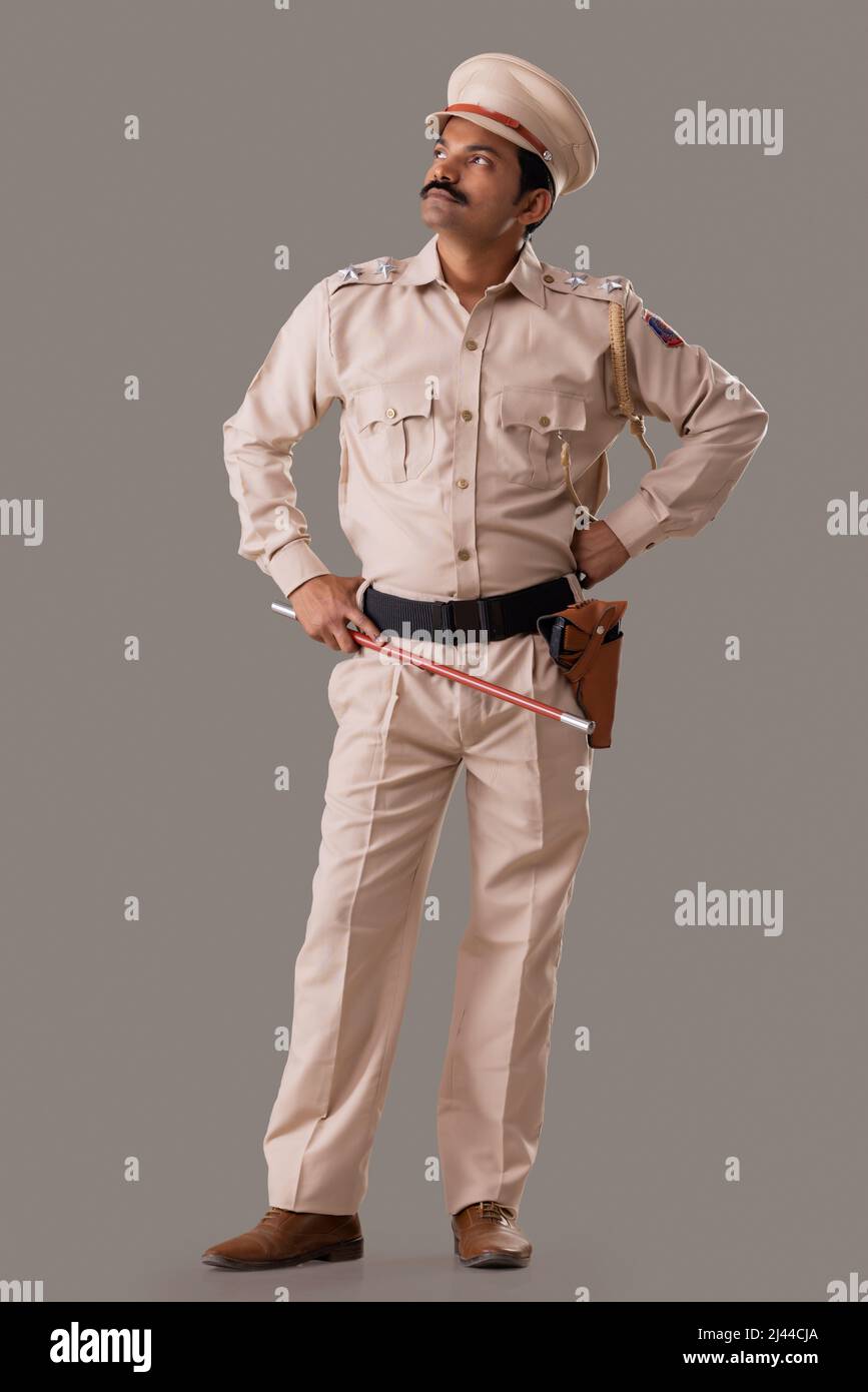 Portrait of an Indian policeman looking elsewhere with baton and hands ...
