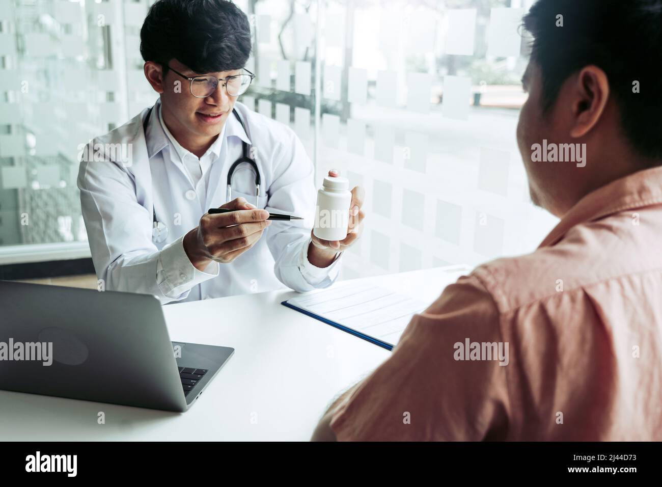 Confident doctor man holding a pill bottle while talking with a senior ...