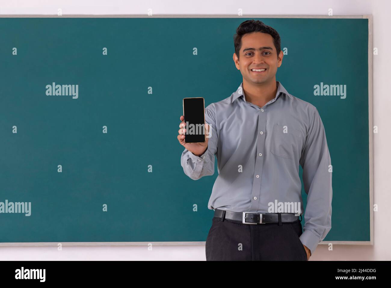 School teacher showing Smartphone while standing in front of blackboard ...