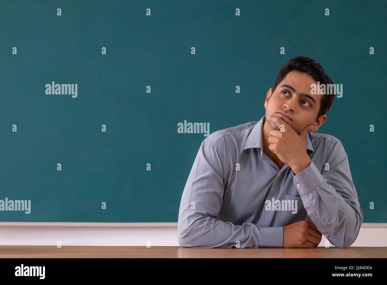 Portrait of a school teacher thinking with hand on chin while sitting ...