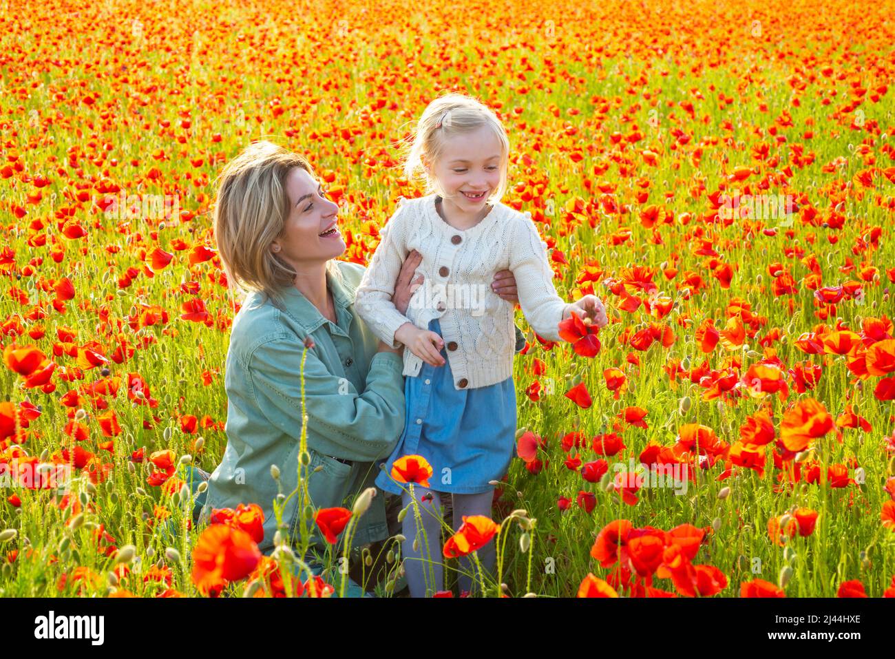 Mother and daughter are playing in the field of flowering red poppies ...