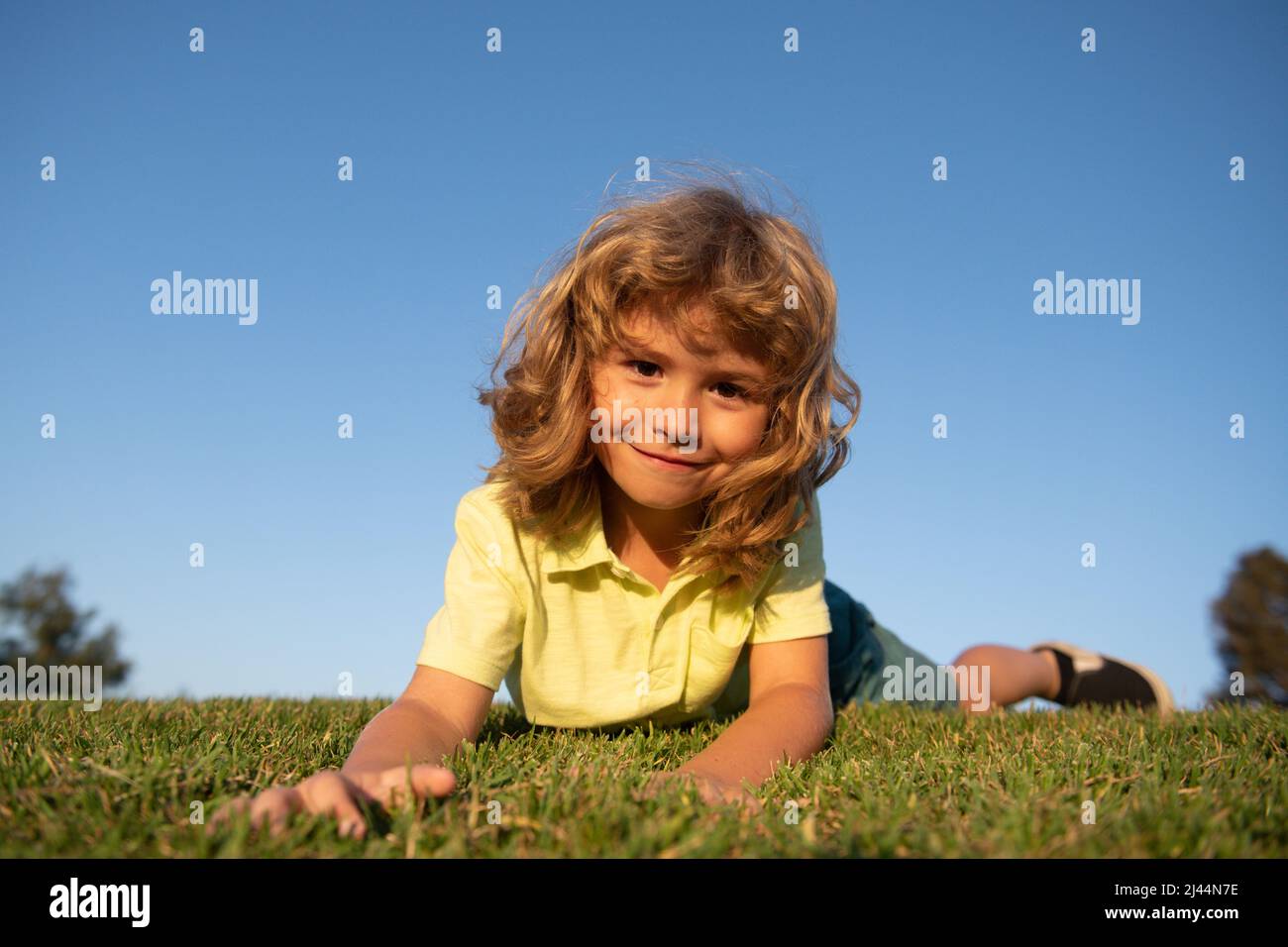 Kid boy laying on the green grass. Happy child playing in green spring ...