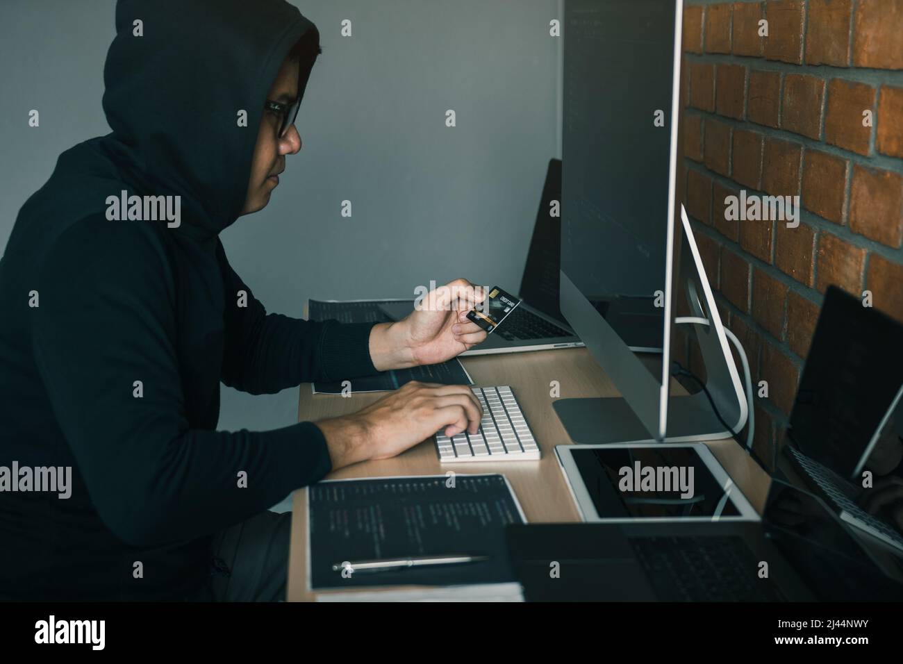 Hacker in the hood working with computer and holding credit card with ...