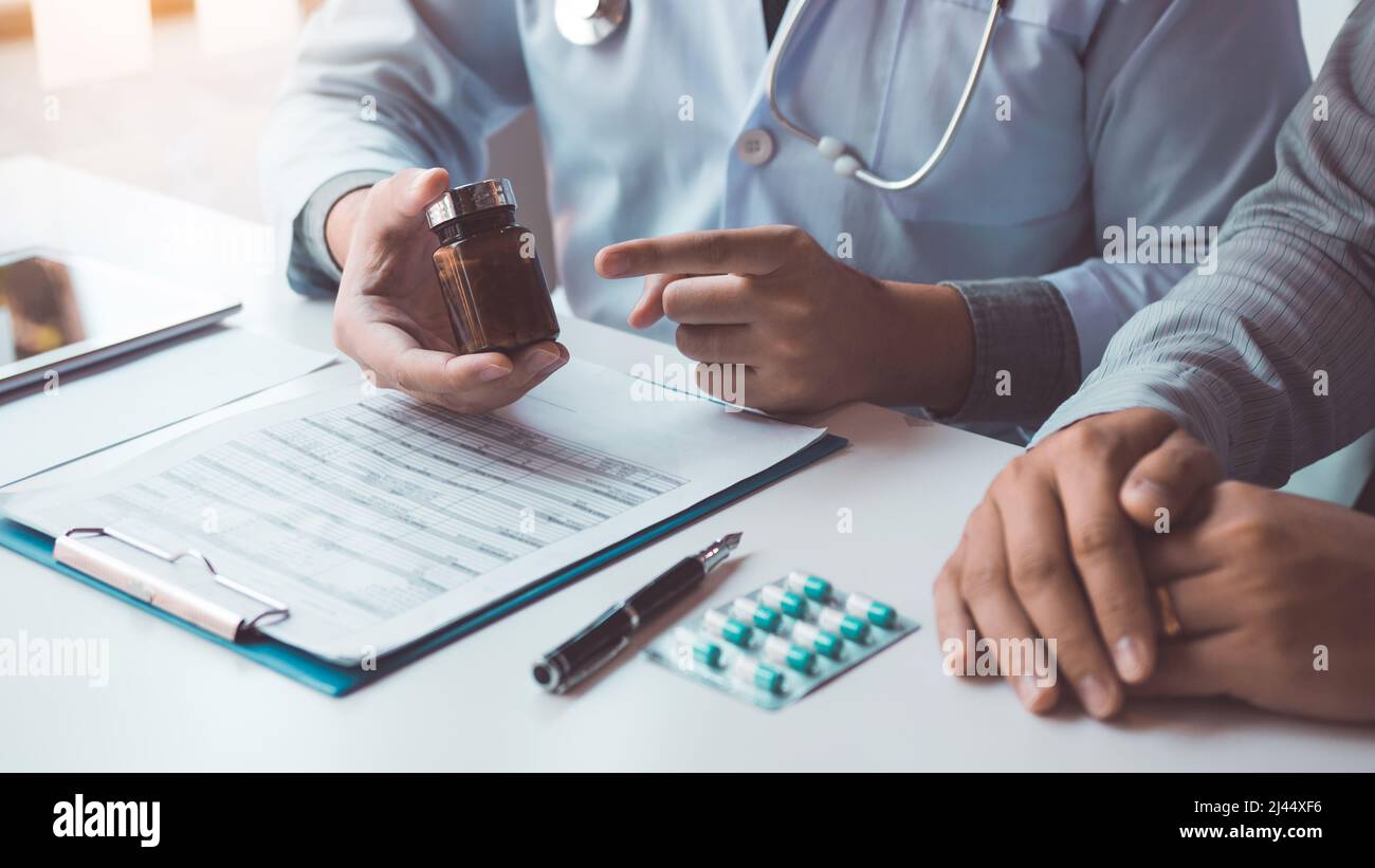 Confident doctor man holding a pill bottle and writing while talking ...