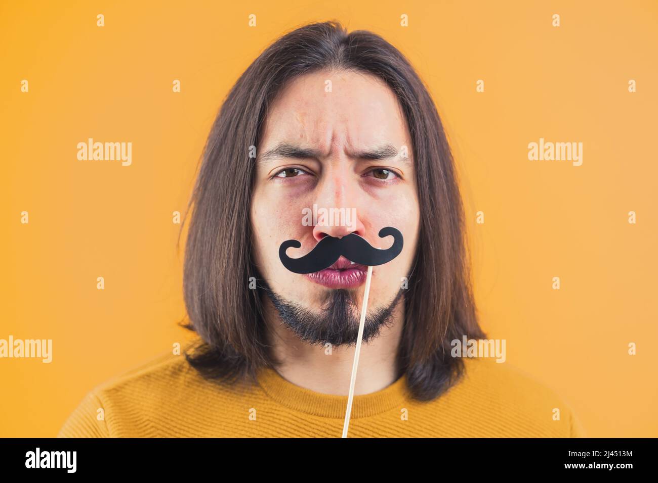 Movember concept - young frowned man holds fake paper moustache on a ...