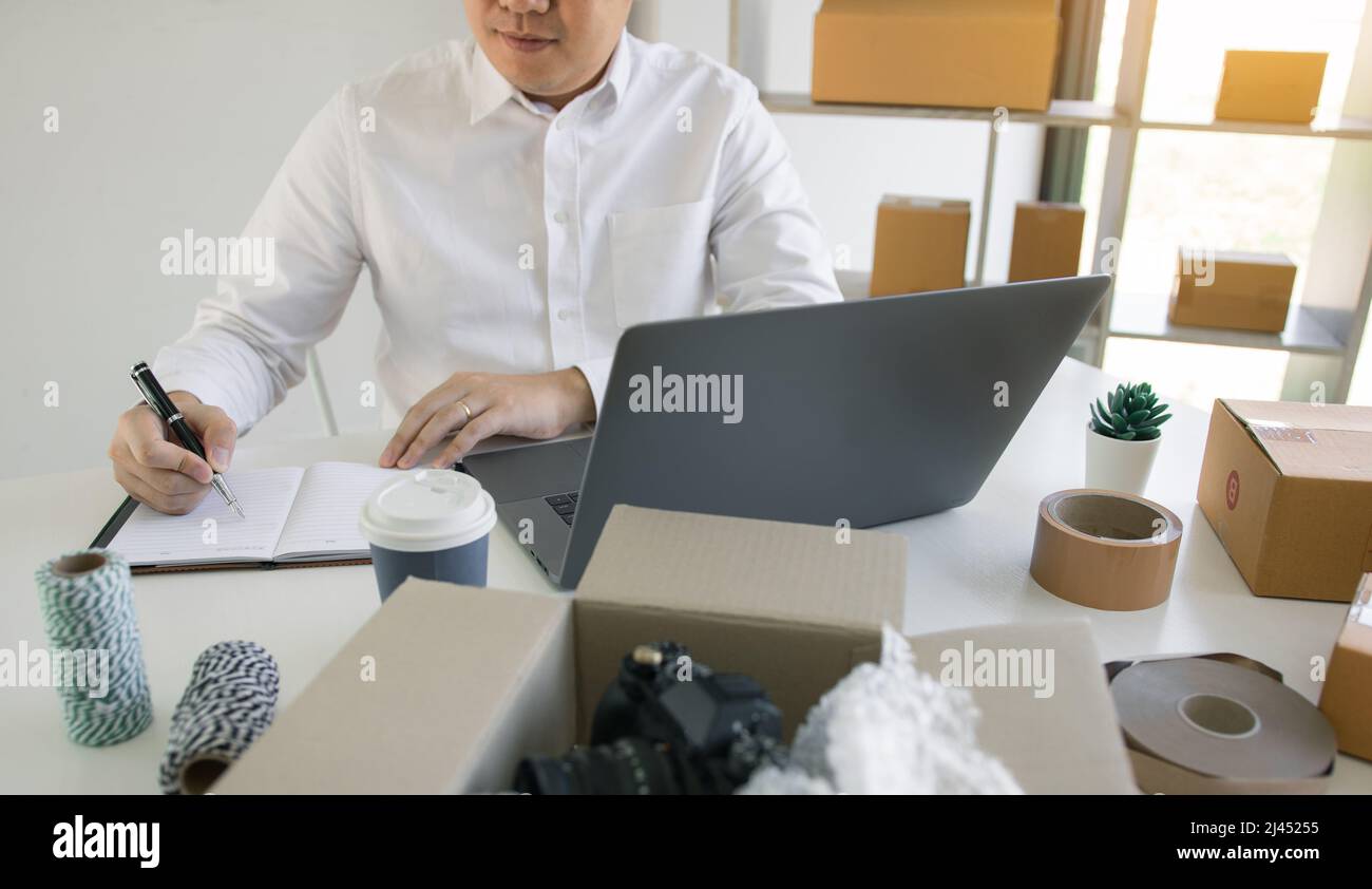 Young asian man looking on computer laptop and taking writing order ...