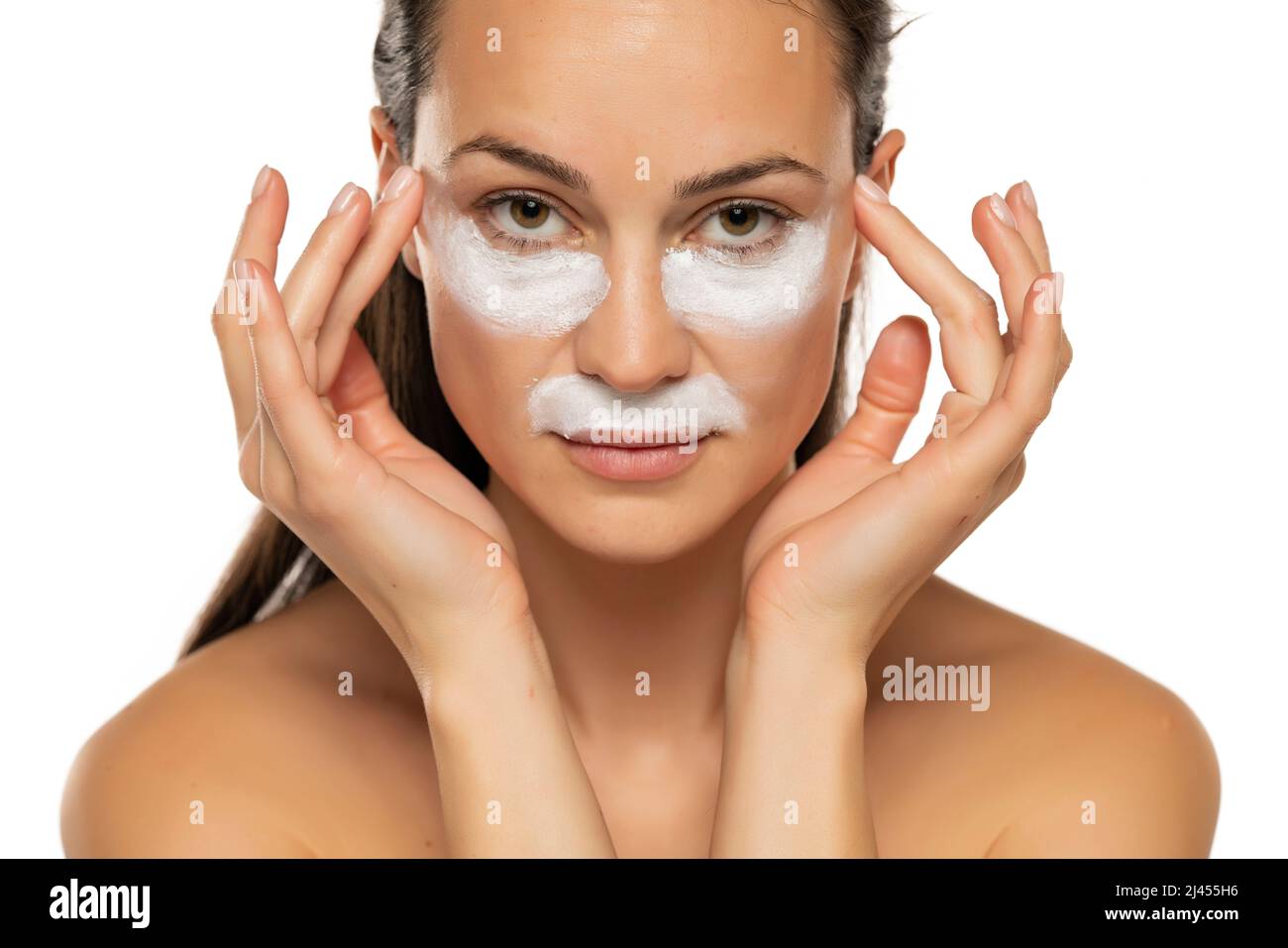 young woman apply cosmetic product on her face on a white background ...