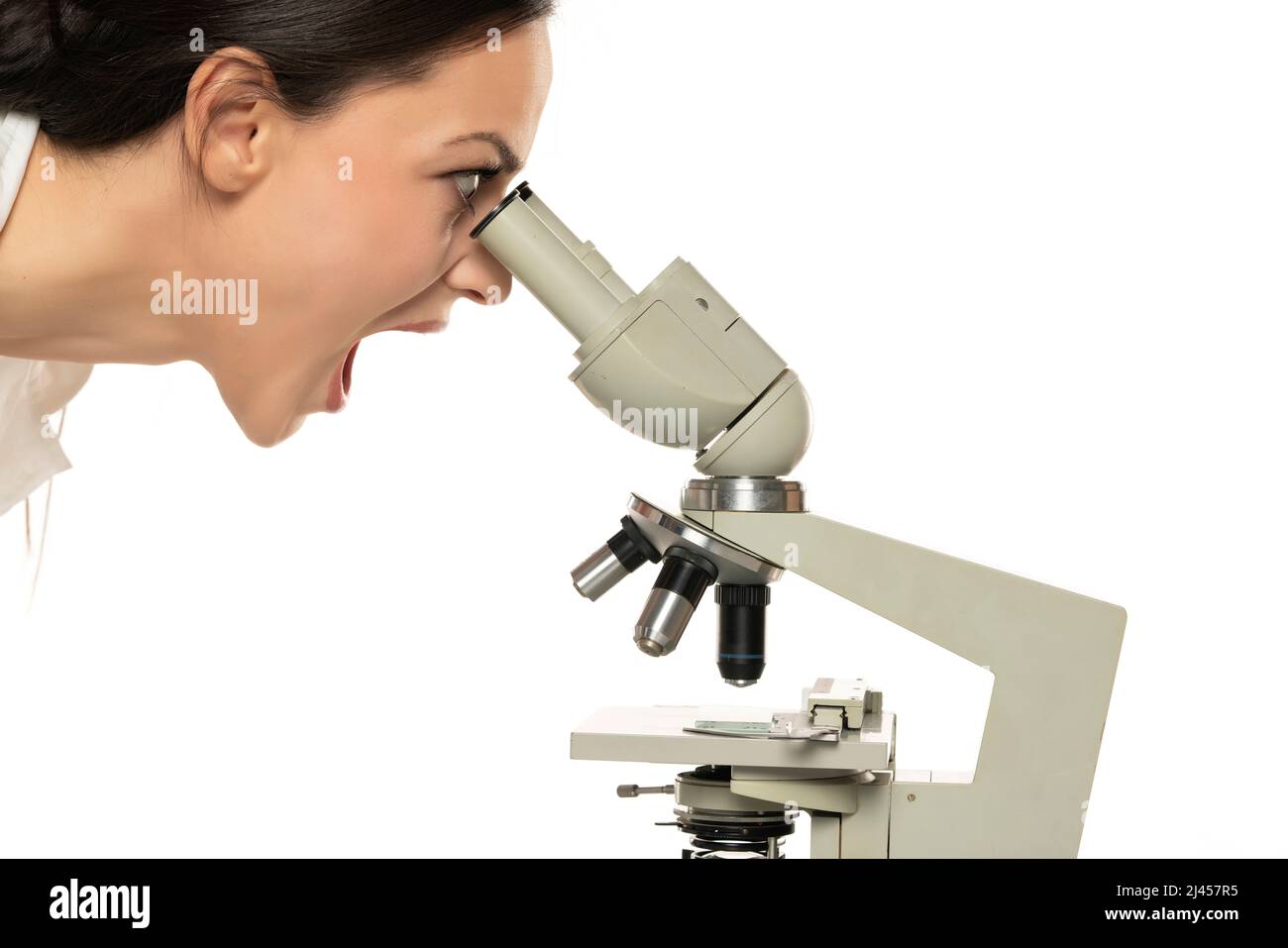 Female angry nervous scientist looking through a microscope, close up ...