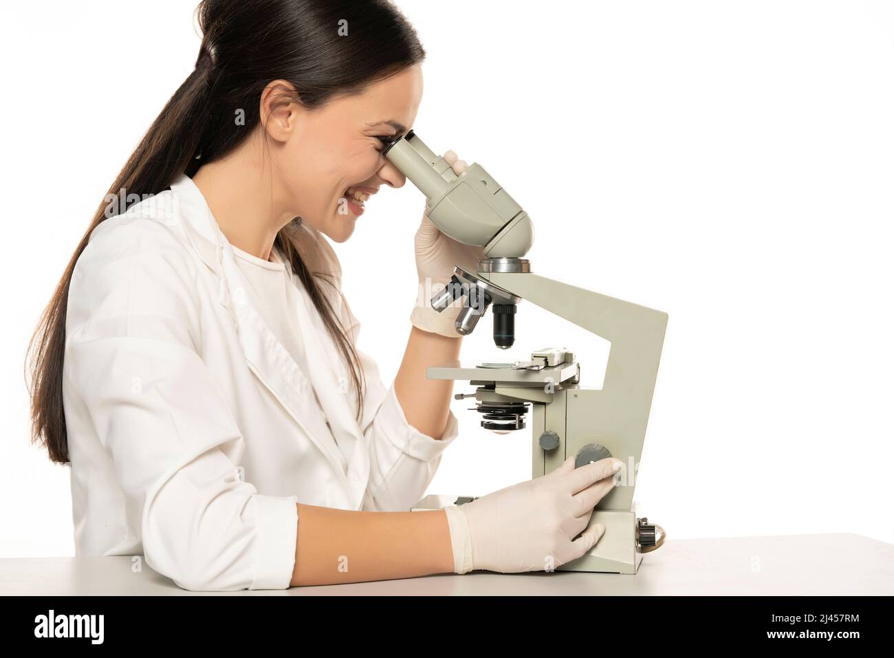 Happy female scientist looking through a microscope, white background ...