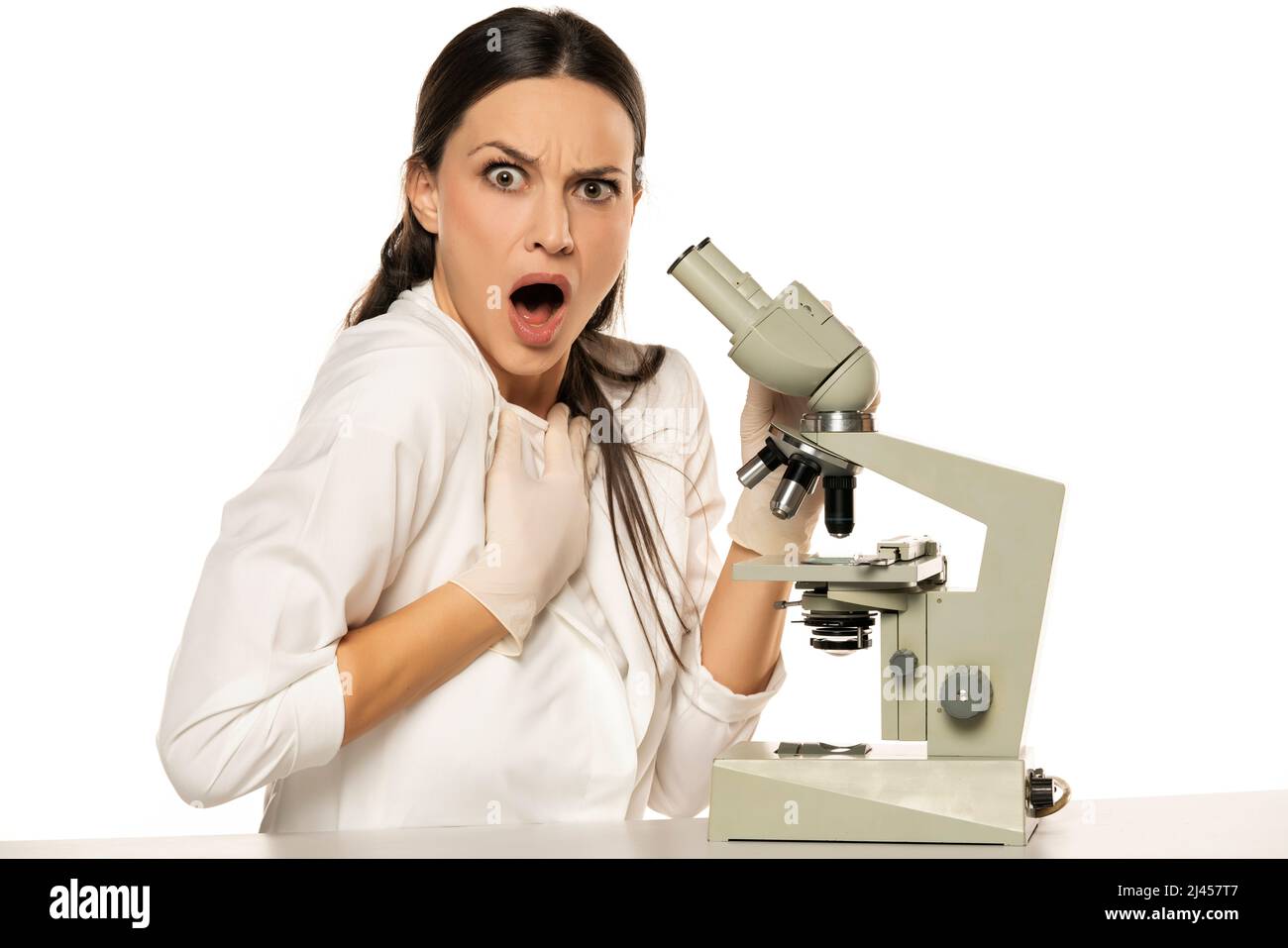 Portrait of shocked female scientist with microscope on a white ...