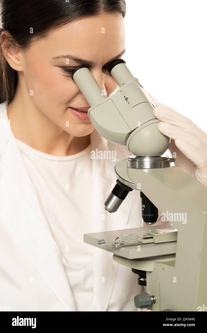 Female smiling scientist looking through a microscope, close up, white ...