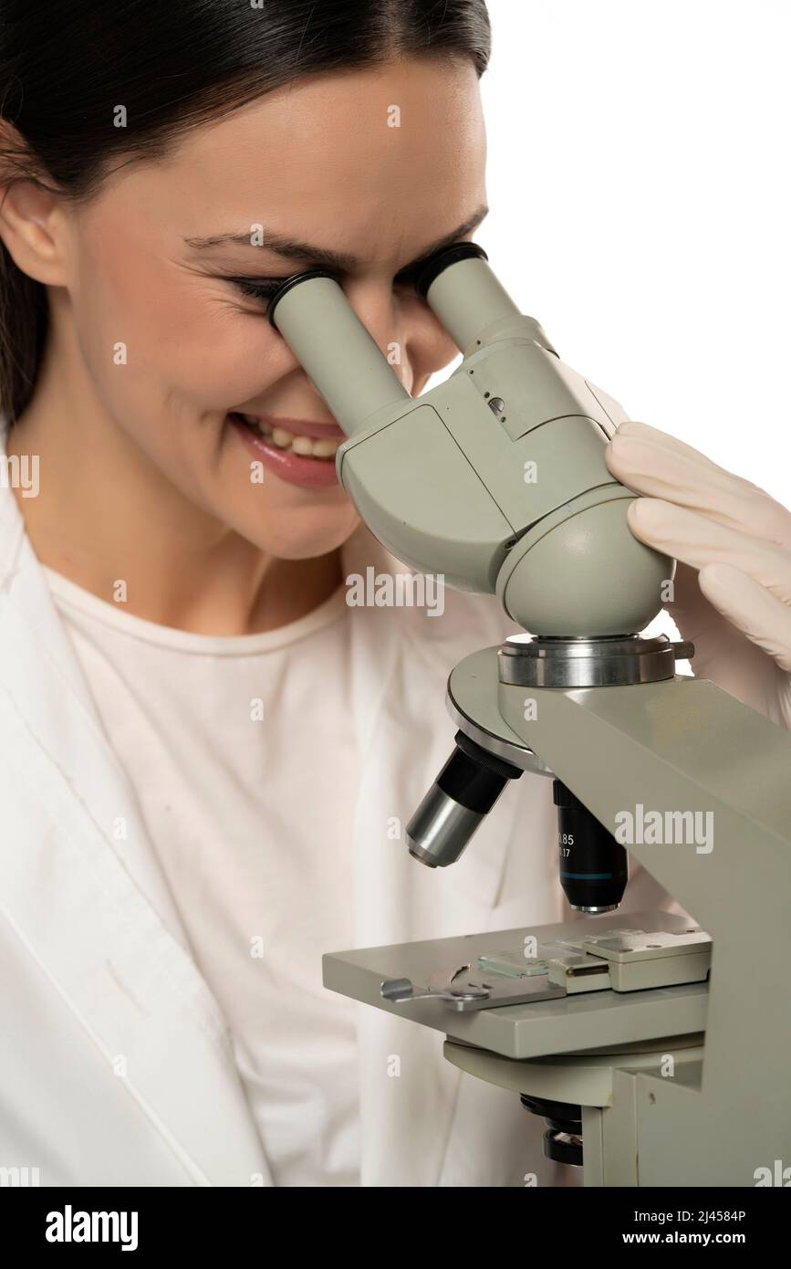 a young smiling female scientist looks through a microscope in a studio ...