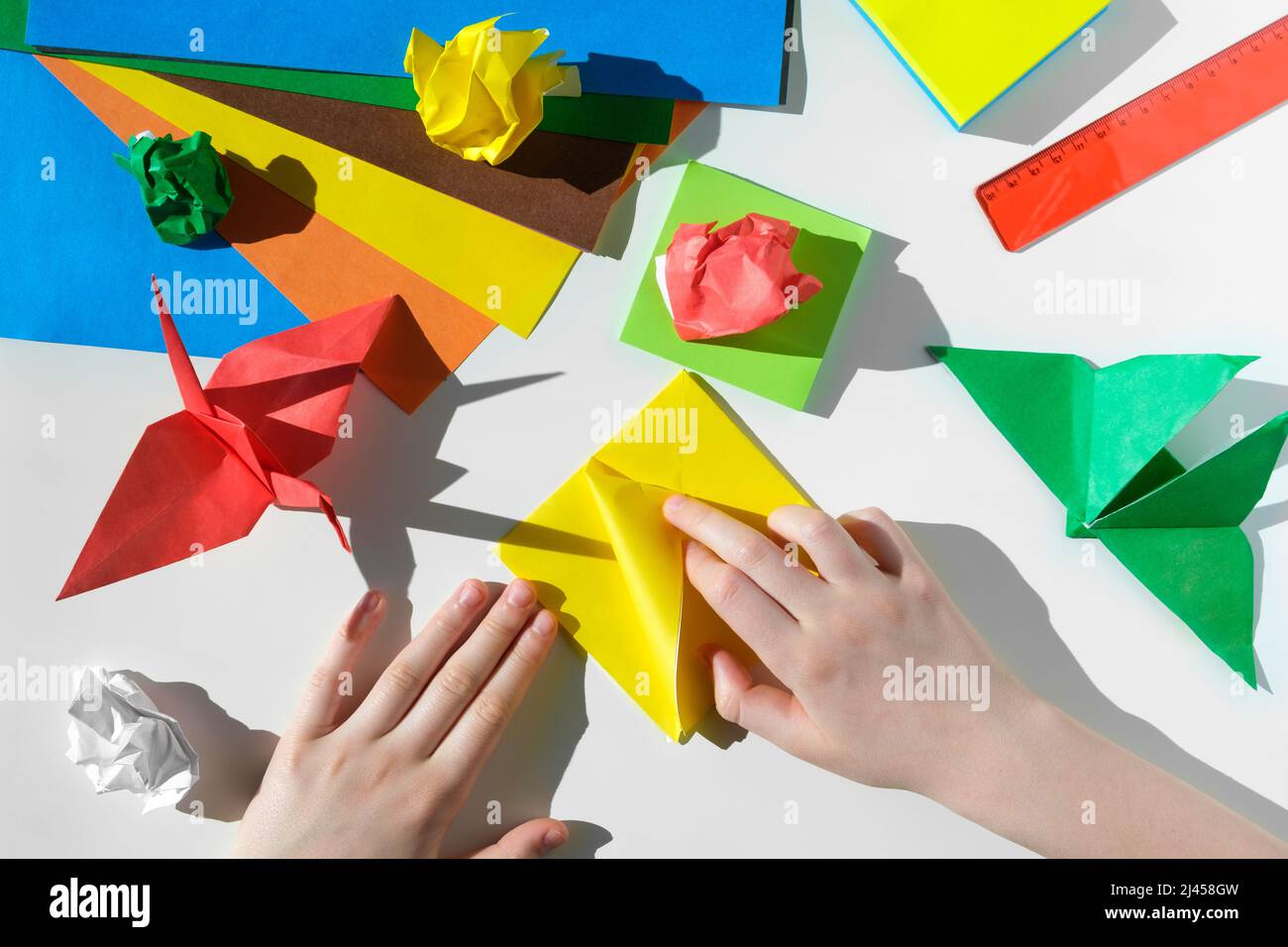 Paper crafts, scissors, colored paper sheets and scraps, on white table ...