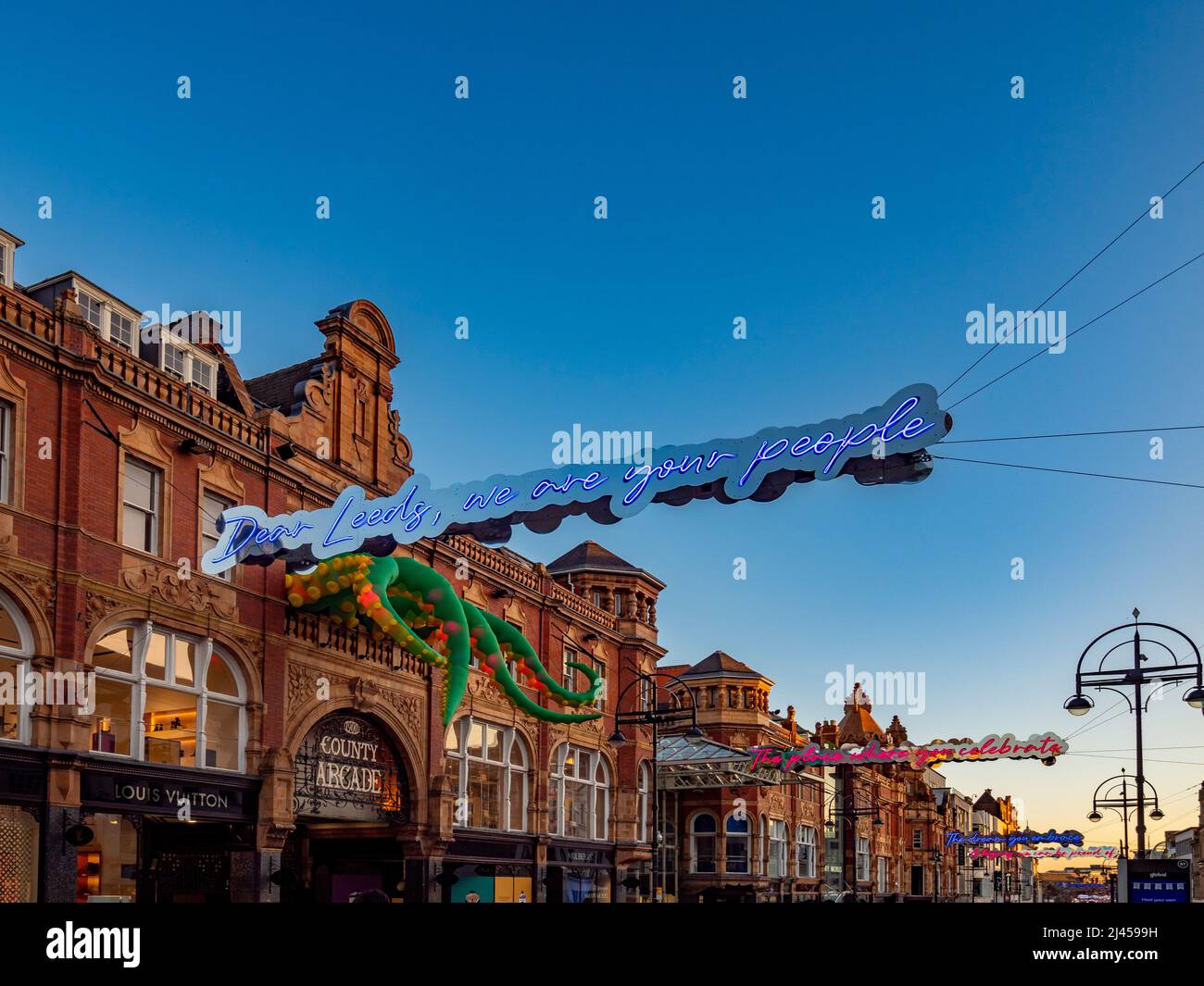 Illuminated neon signs suspended across Briggate, at dusk. Leeds UK ...