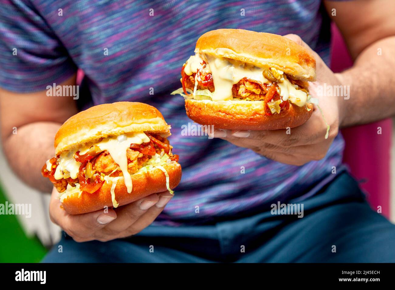 Man holding two spicy fried chicken burger oozing with melted cheese ...