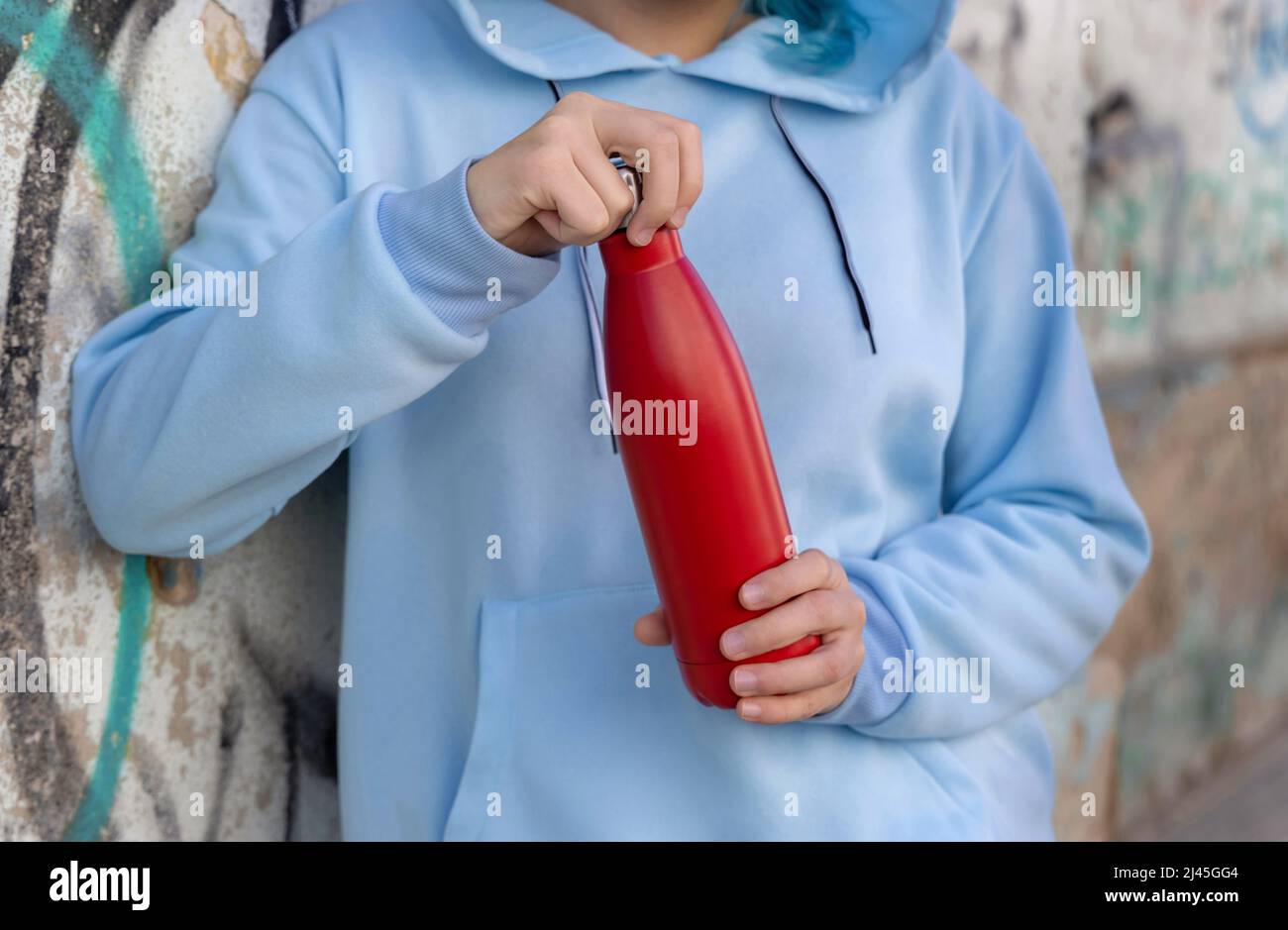 Young woman in blue hoodie with red water bottle staying outdoors near ...