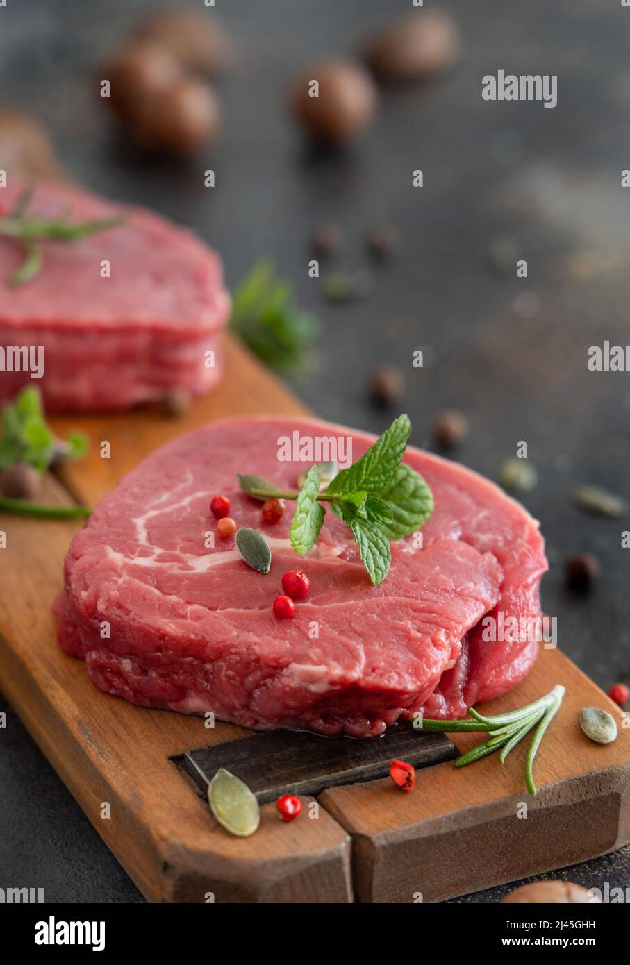 Raw beef fillet steaks on wooden board on dark background close up ...