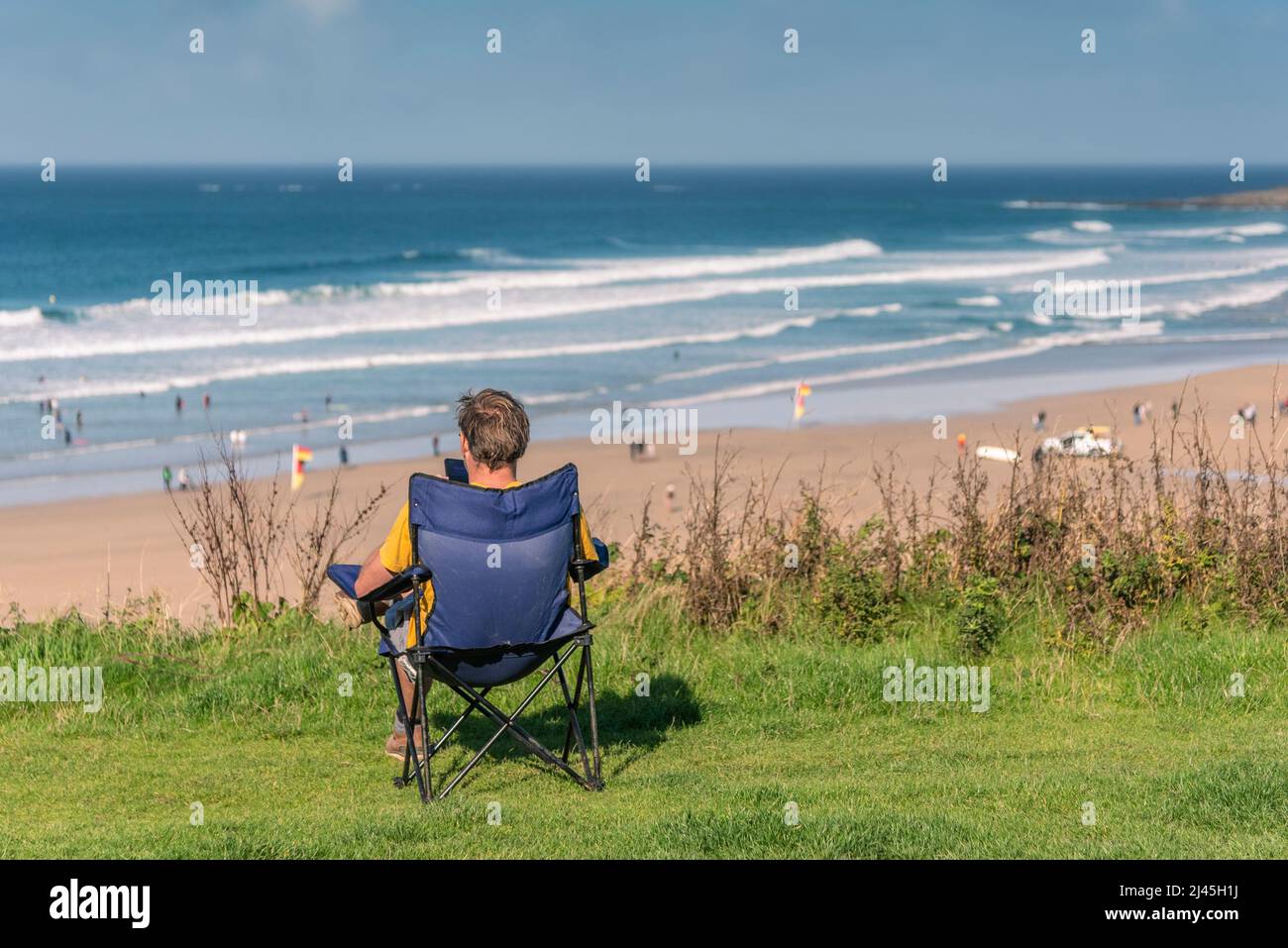 A male holidaymaker sitting and relaxing in a camping chair overlooking ...