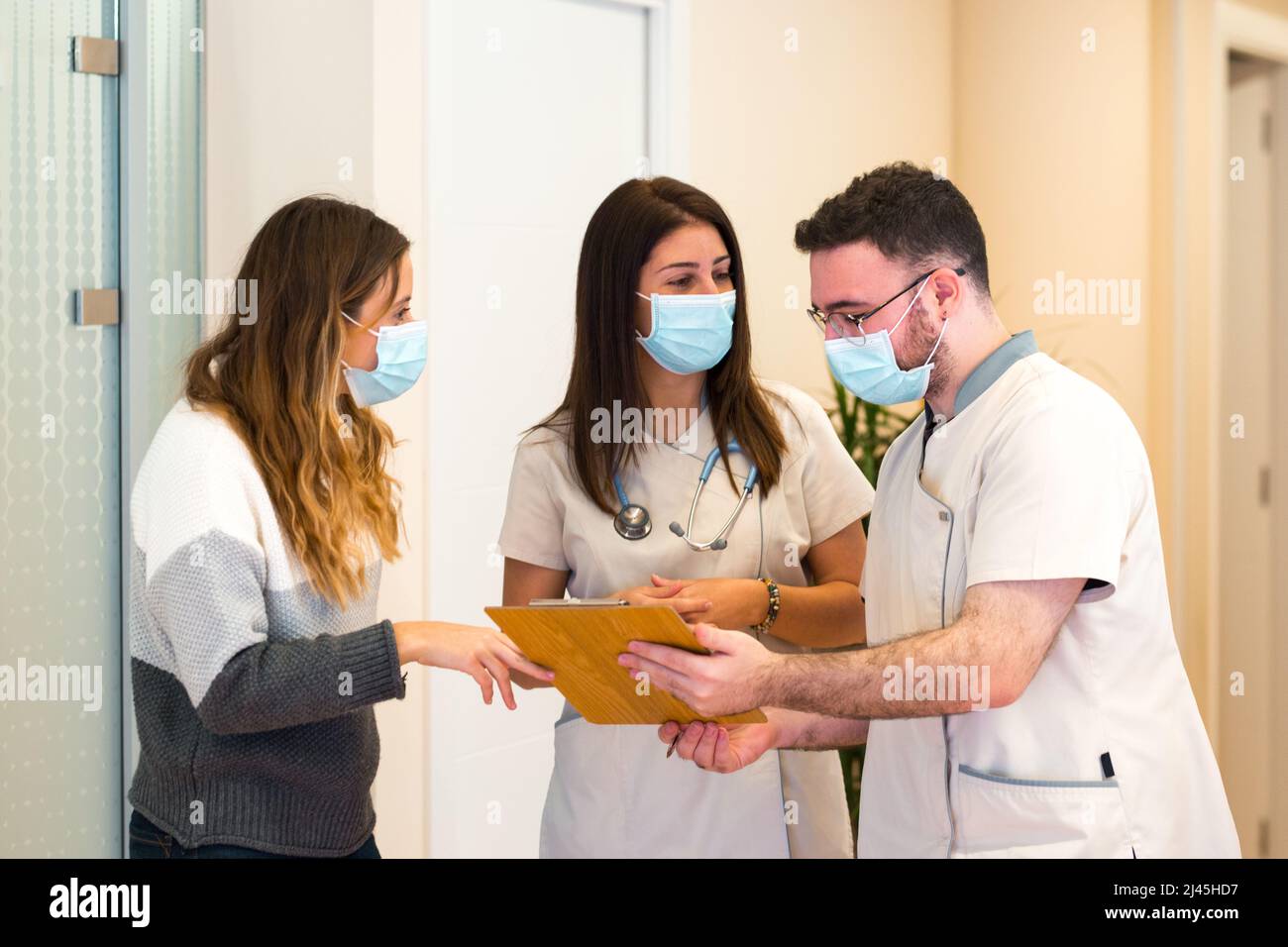 Two doctors discussing notes on clipboard together with female patient ...