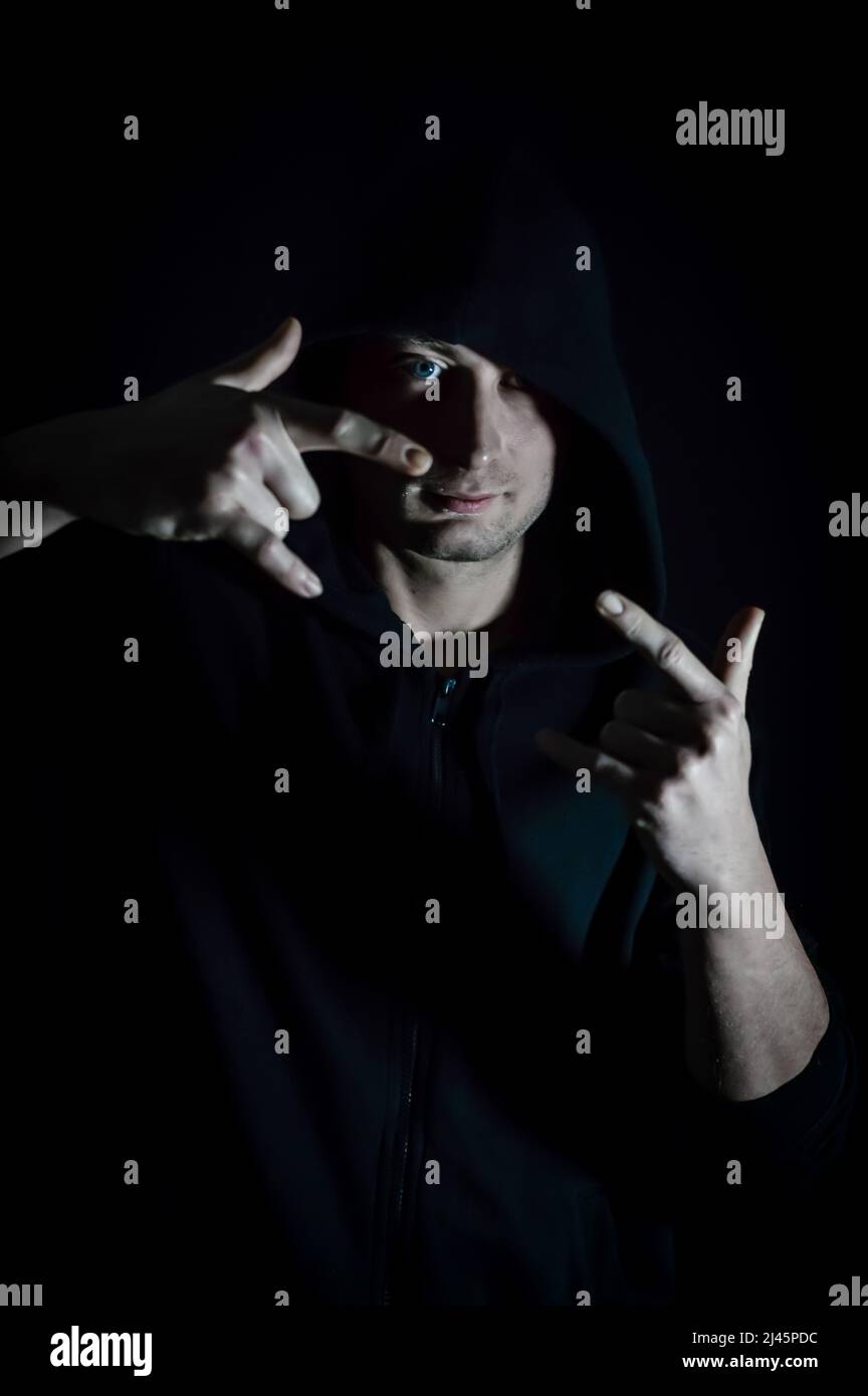 Portrait of a young hooded man making a sign of the horns with both ...
