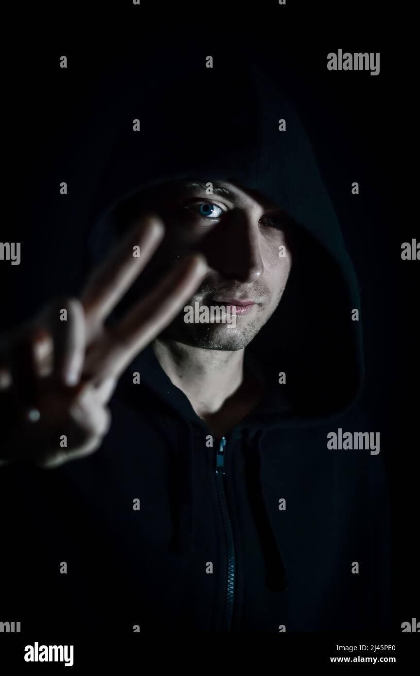 Portrait of a young hooded man making a victory sign with his fingers ...