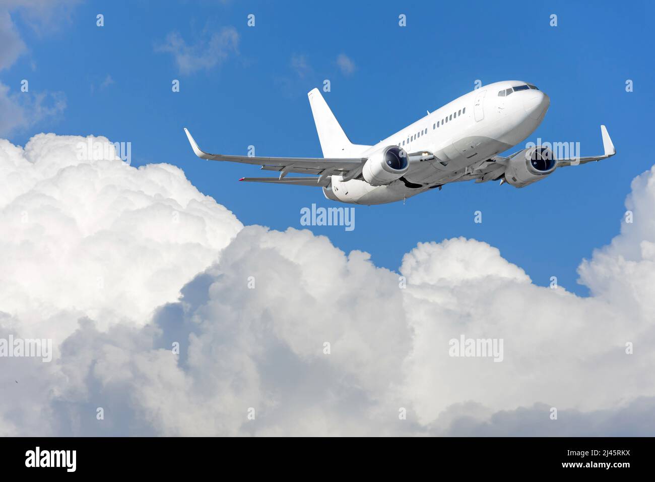 Climbing plane flies over the tops of cumulus clouds in the blue sky ...