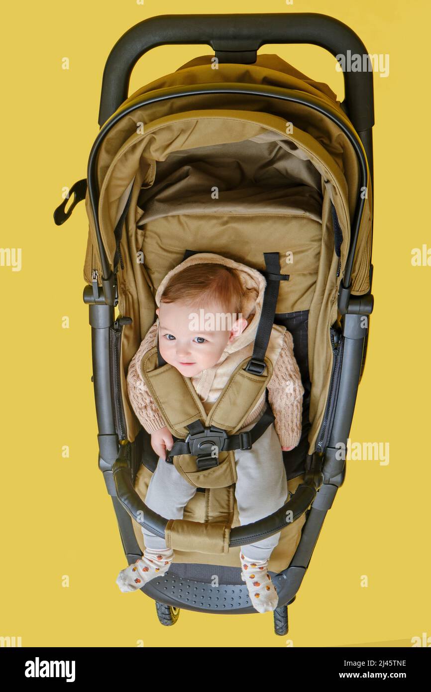 A happy child is sitting in a baby carriage on a studio yellow ...
