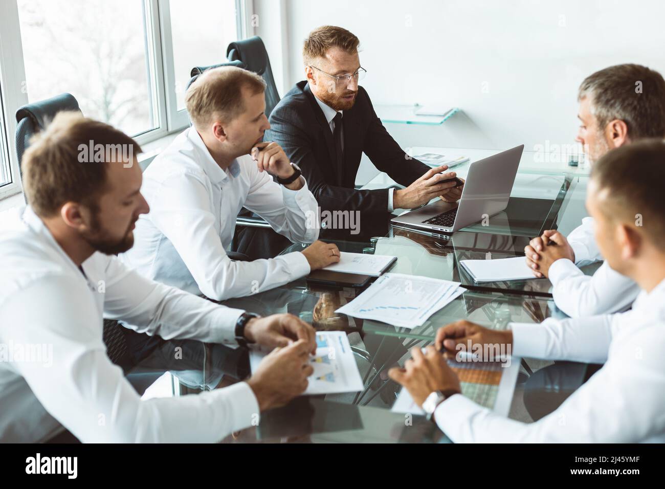 A group of company employees sits at a table in a meeting room. A team ...