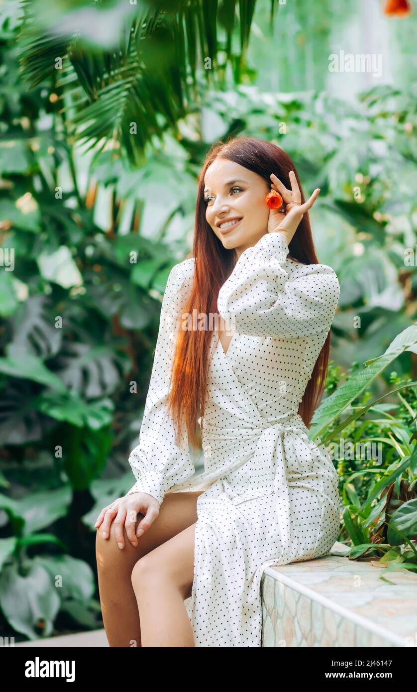 Cute girl with long red hair posing in a greenhouse among tropical plants Stock Photo - Alamy
