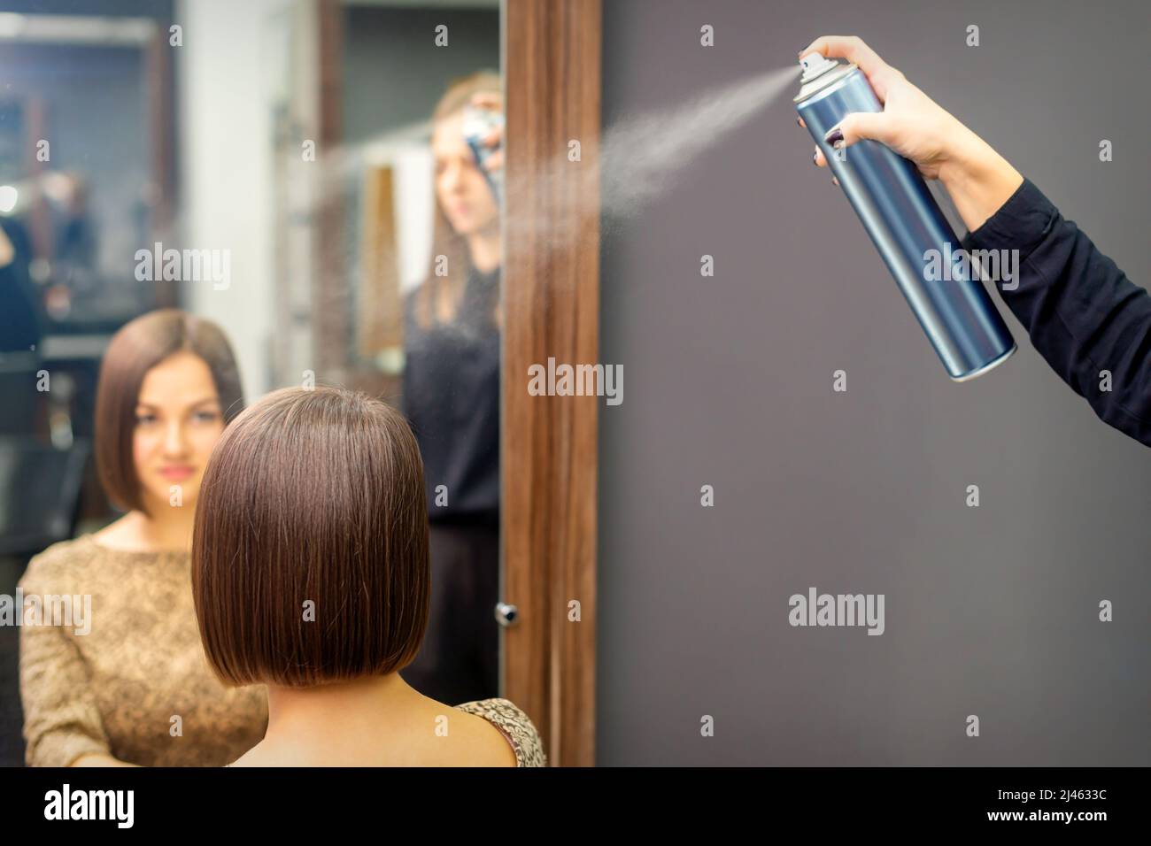 A hairdresser is using hair spray to fix the short hairstyle of the ...
