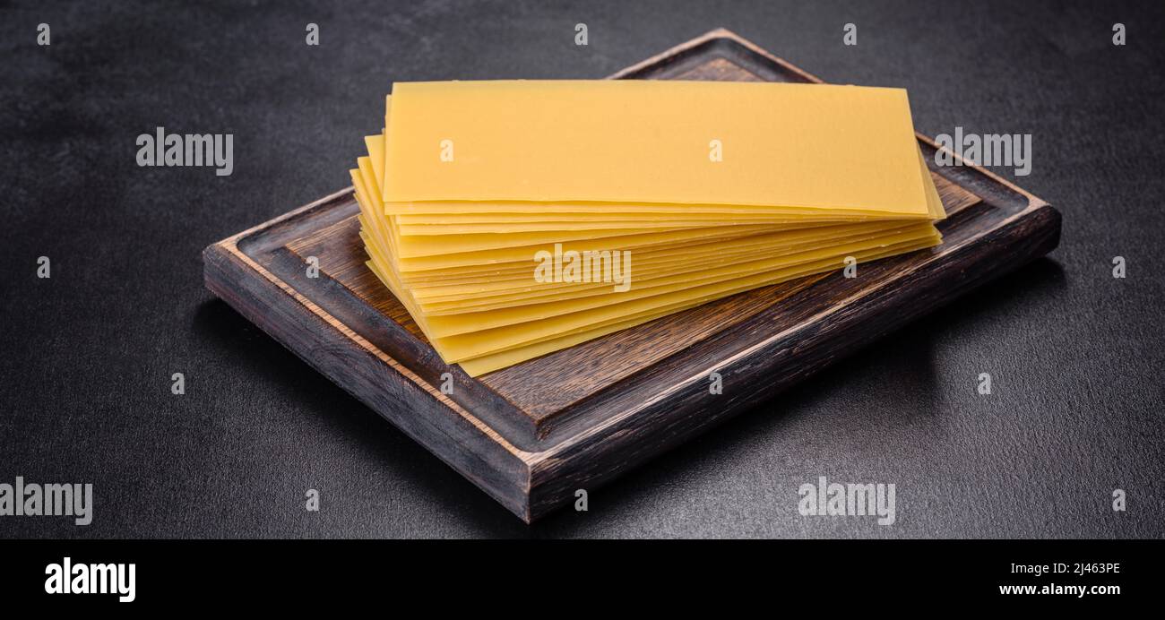 A stack of raw lasagna sheets with herbs and spices on a dark concrete ...