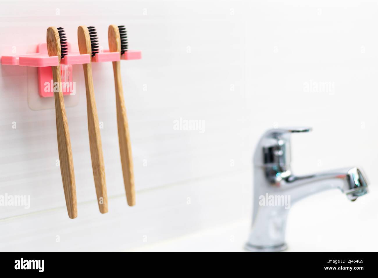 Three natural bamboo toothbrushes with black bristles in a holder ...