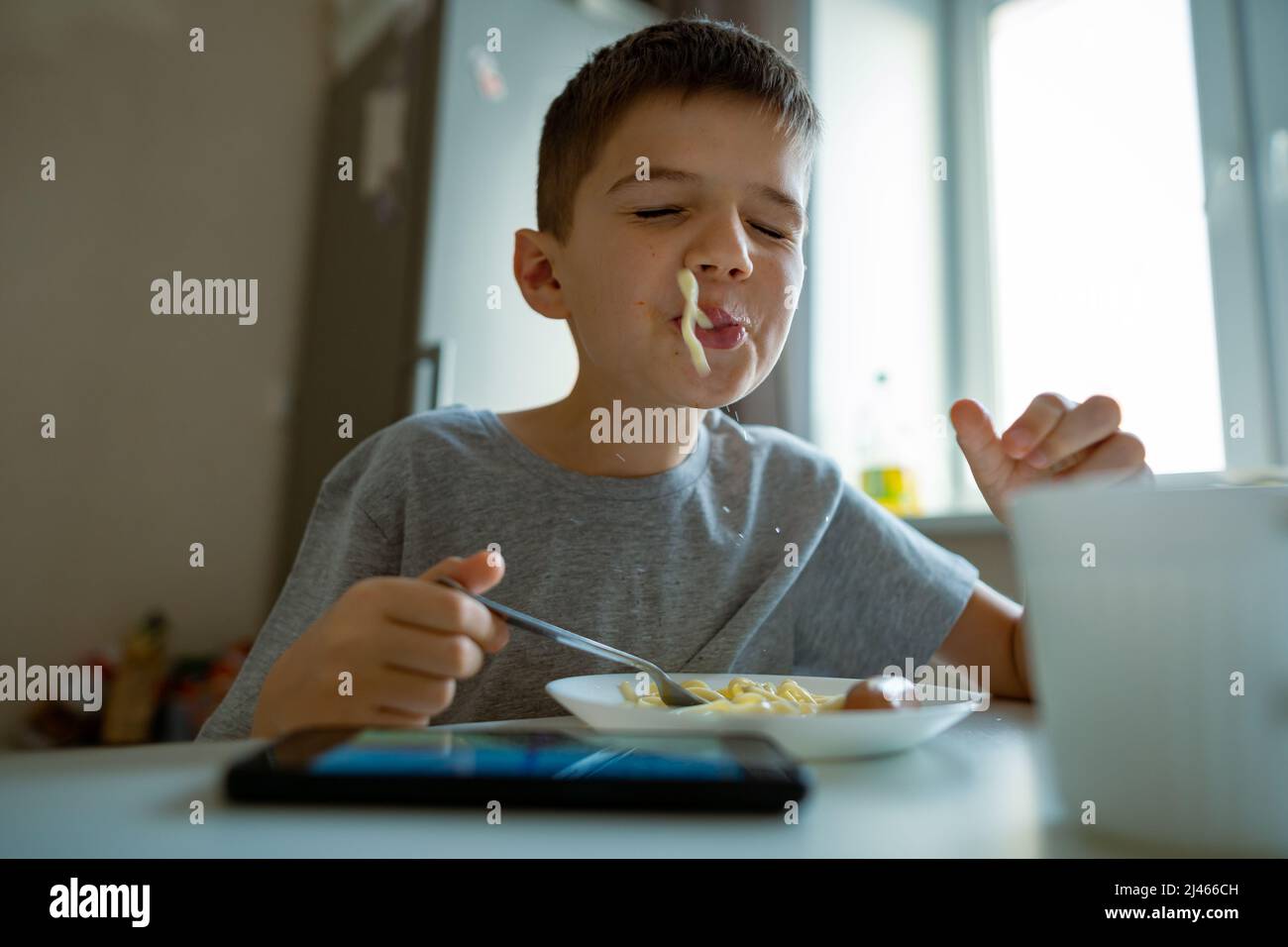 A cheerful, hungry boy eats pasta with appetite. Male Child sucks in ...
