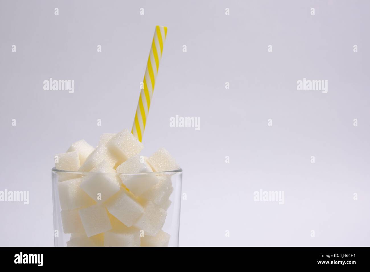 Glass with refined sugar cubes and a drinking tube on a white ...