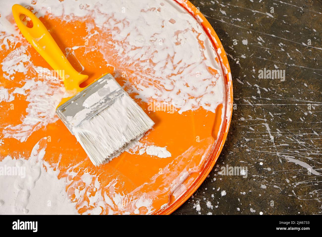 Dirty paintbrush stained with paint lies on an orange lid on floor ...