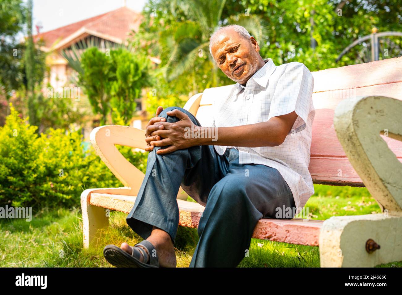Senior old man suffering from knee joint pain while sitting at park ...